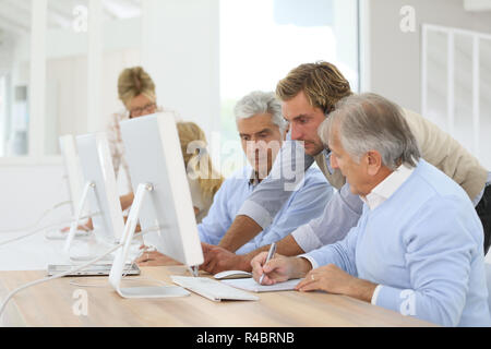 Instructor helping senior men with computing class Stock Photo - Alamy