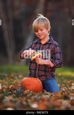 Smiling boy carving a Halloween pumpkin in the garden, United States ...