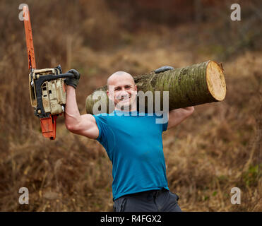 Strong muscular lumberjack with chainsaw, carrying a huge log on his ...
