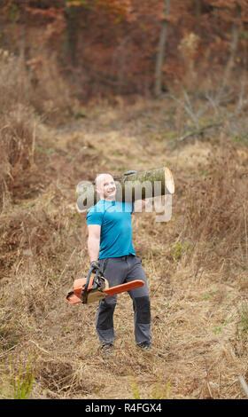 Strong muscular lumberjack with chainsaw, carrying a huge log on his ...
