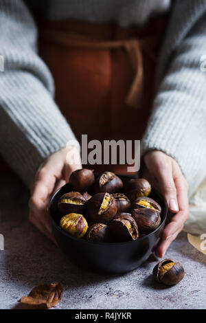 Hands holding roasted chestnuts on a wooden table with also chestnut ...