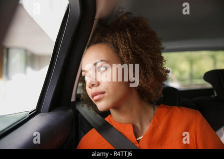 Woman riding in a car, looking at her smartphone and holding a reusable ...