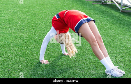 A high school cheerleader is in a bridge while warming up doing a back ...