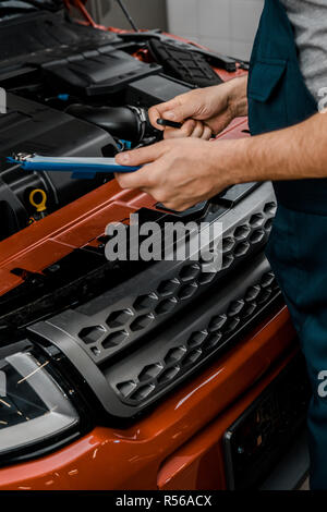 partial view of auto mechanic with notepad examining new car at auto ...
