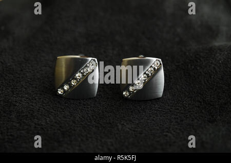 Silver cufflinks with rhinestones on a black background next to the ...