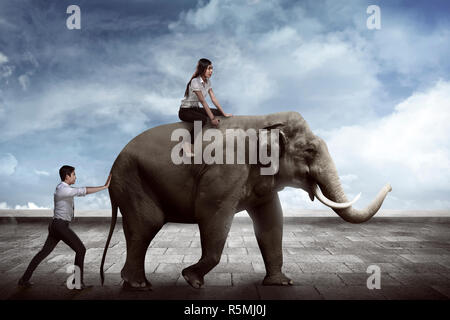 Asian business man push elephant while his friend sit on it back Stock ...