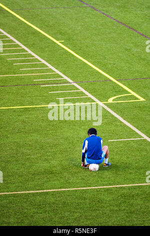 Unhappy teenage boy excluded from the soccer team sits on the ball at ...