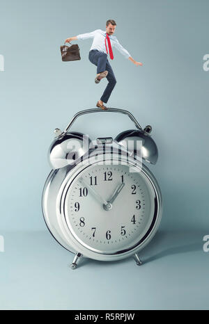 Jumping young businessman with alarm clock instead of his head on ...