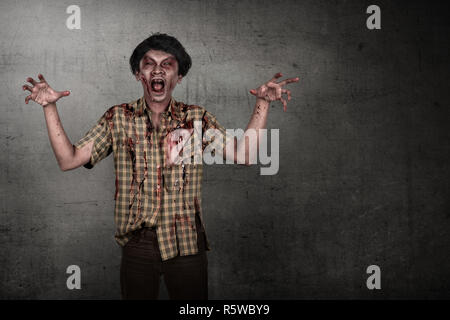 Aggressive asian zombie man with angry face over dirty wall background ...