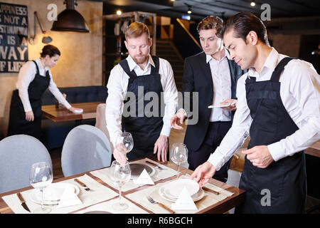 Serious banquet manager and waiters serving tables for event. Handsome ...