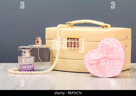 Cosmetic bag, bottles of perfume and gift box on wooden boards and gray ...