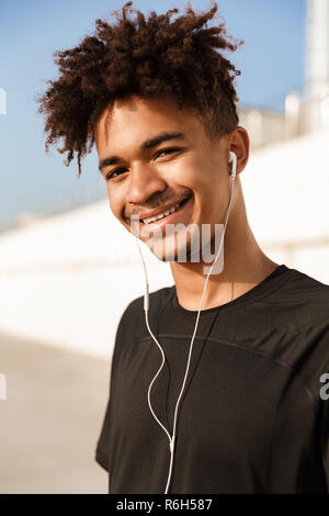 Smiling young african teenager sportsman standing at the beach, taking ...