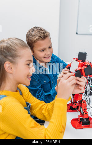 smiling schoolchildren programming robot together during STEM ...