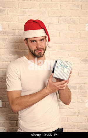 Macho in santa hat present on white brick wall. Man hold red jewelry ...