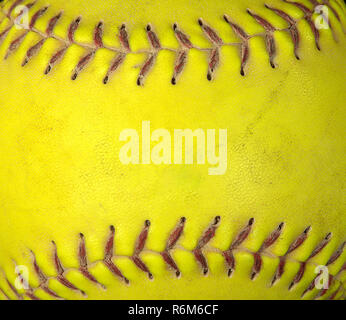 Bright yellow softball with red seams sitting inside white glove mitt ...