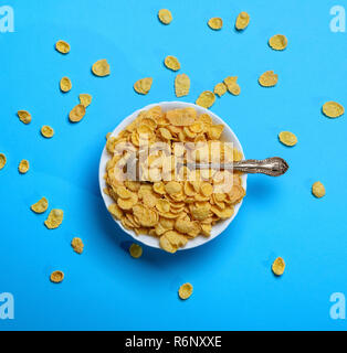 cornflakes in a white ceramic plate and an iron spoon on a blue ...
