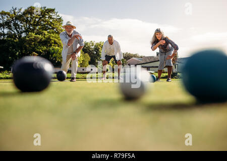 Senior man playing bocce ball with a senior woman sitting on a chair ...