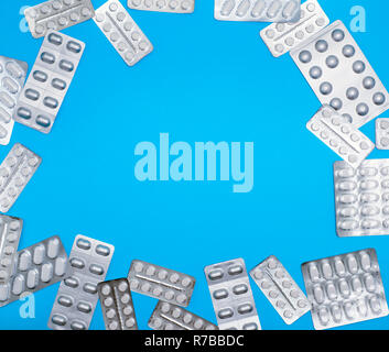 different white tablets in a package are scattered on a blue background ...