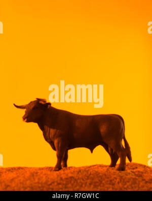 Toy bull against orange-yellow glowing sunset type backdrop. Metaphor ...