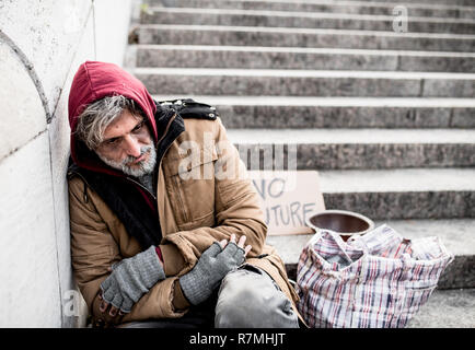 Homeless Man In Hood Sitting On Street Holding Cardboard With Text ...
