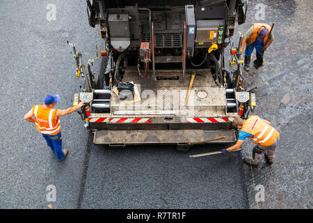 An asphalt laying machine and men at work resurfacing the road in Brook ...