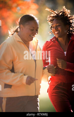 Two women running next to each other in a park with green trees Stock ...