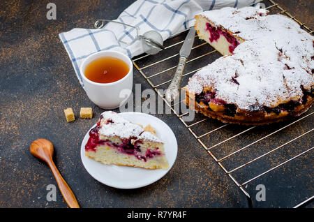 Cherry or plum pie sprinkled with icing sugar, cup of tea on dark ...