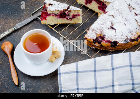 Cherry or plum pie sprinkled with icing sugar, cup of tea on dark ...