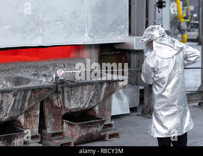 a worker taking a sample of molten aluminum from the inside of a big ...