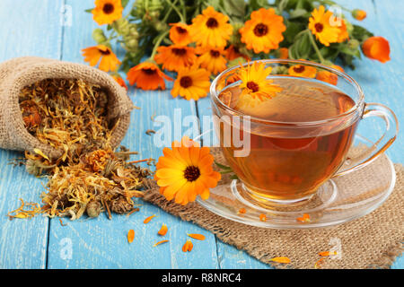 Calendula tea with fresh and dried flowers on blue wooden background ...