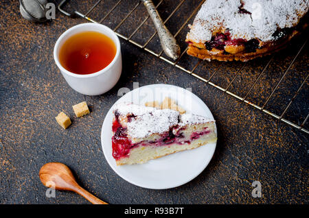 Cherry or plum pie sprinkled with icing sugar, cup of tea on dark ...