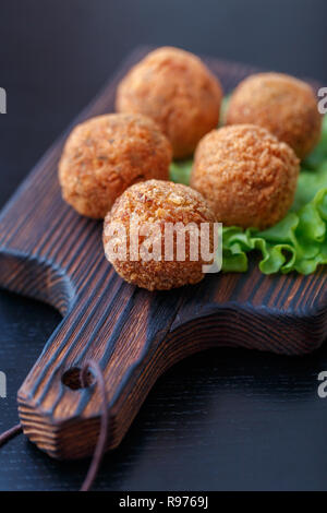Falafel lies on a wooden cutting board. On the table lie tomatoes ...