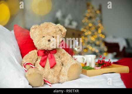 Two teddy bears siting on the bed with red candys near christmas tree ...
