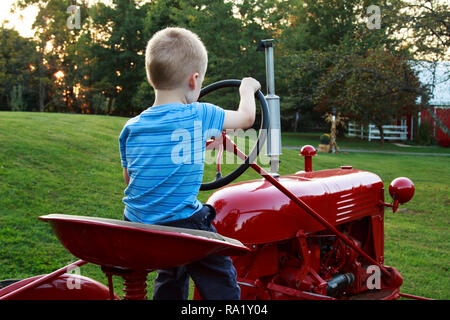 Toddler boy in the garden pretending to be a farmer driving a tractor ...