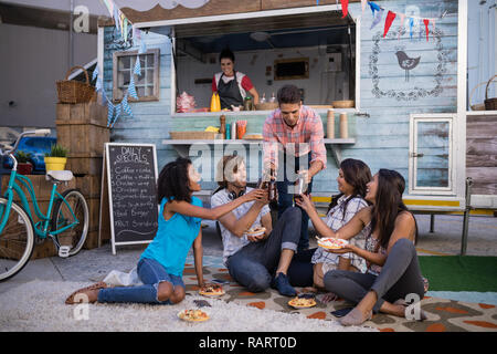 Smiling young man passing beer bottles from window to friends standing ...
