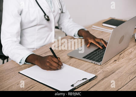 cropped view of scientist typing on laptop in laboratory near blurred ...