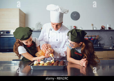 Cute girls in aprons and hats reading recipe book together while ...