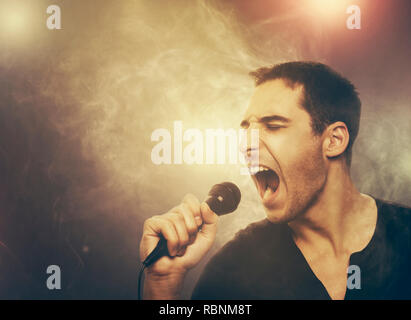 The young guy vocalist is screaming in microphone on stage on concert ...