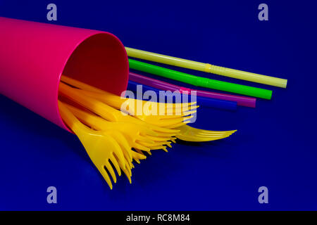 A pile of yellow plastic forks in a plastic pink mug and colored straws ...