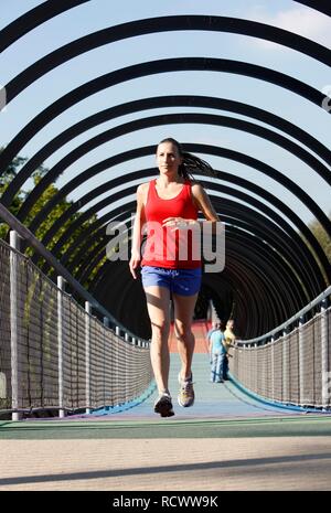 Female jogger, runner, on a pedestrian bridge. Bridge called "Slinky ...