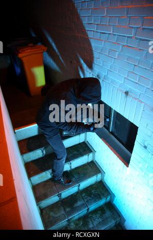 Burglar breaking open cellar window with a crowbar in a cellar corridor ...