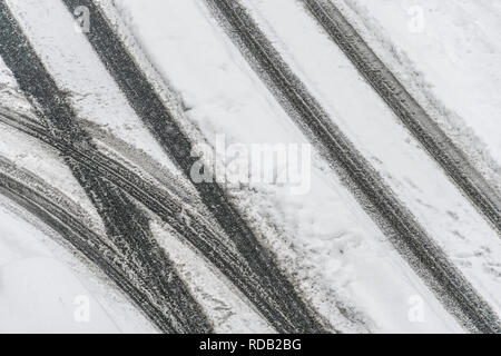 Tire tracks on a snowy road leading into the woods with snow covered ...
