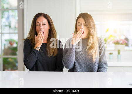 Hispanic mother and daughter together yawning tired covering half face ...