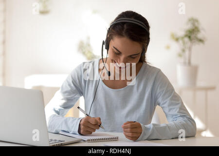 freelancer in headphones writing in notebook near laptop and smartphone ...