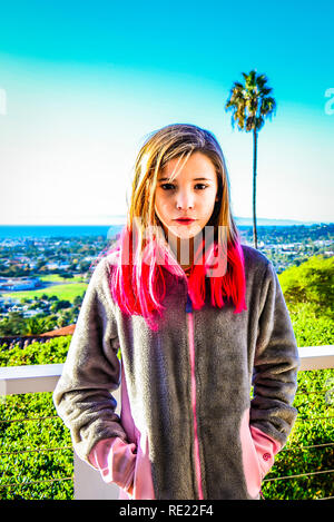 Happy tween with trendy pink hair, smiles while leaning on balcony rail ...