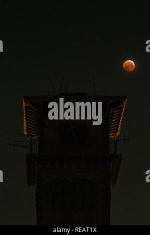 Full blood red moon in a city sky, tv antennas are visible in the ...