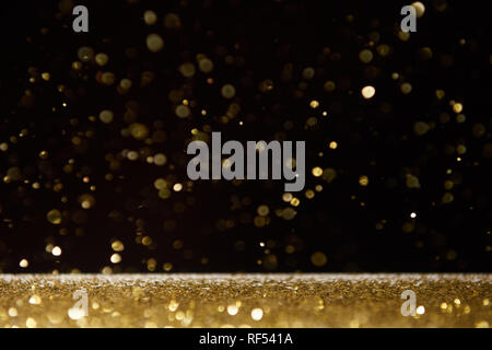 selective focus of golden sparkles falling on table isolated on black ...