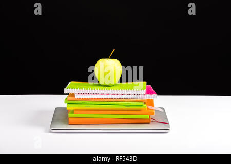 colorful notebooks, apple and laptop on desk isolated on black with ...