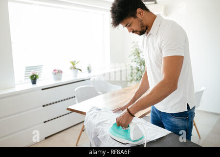 Young man with beard ironing clothes at home angry and mad screaming ...