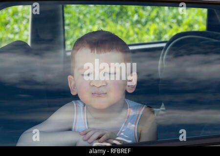 A young boy with his nose pressed against a glass window, indoors ...